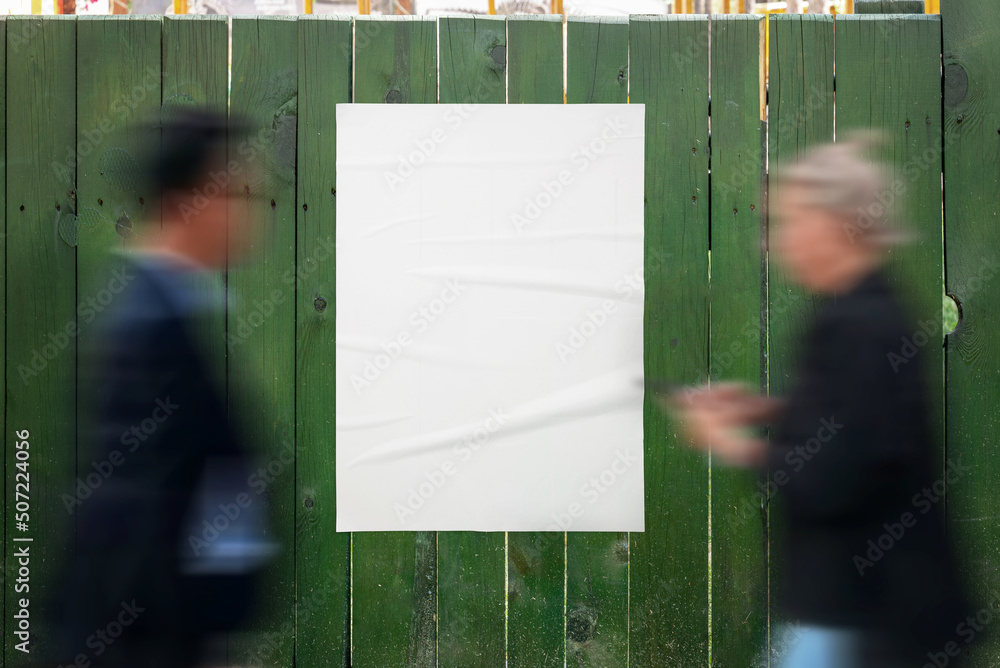Poster mockup on a green wooden fence. People pass by the poster. Blank ...