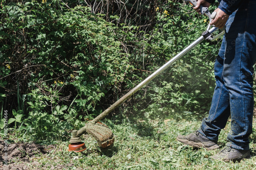 The man mowing green wild grass using brush cutter mower or power tool ...