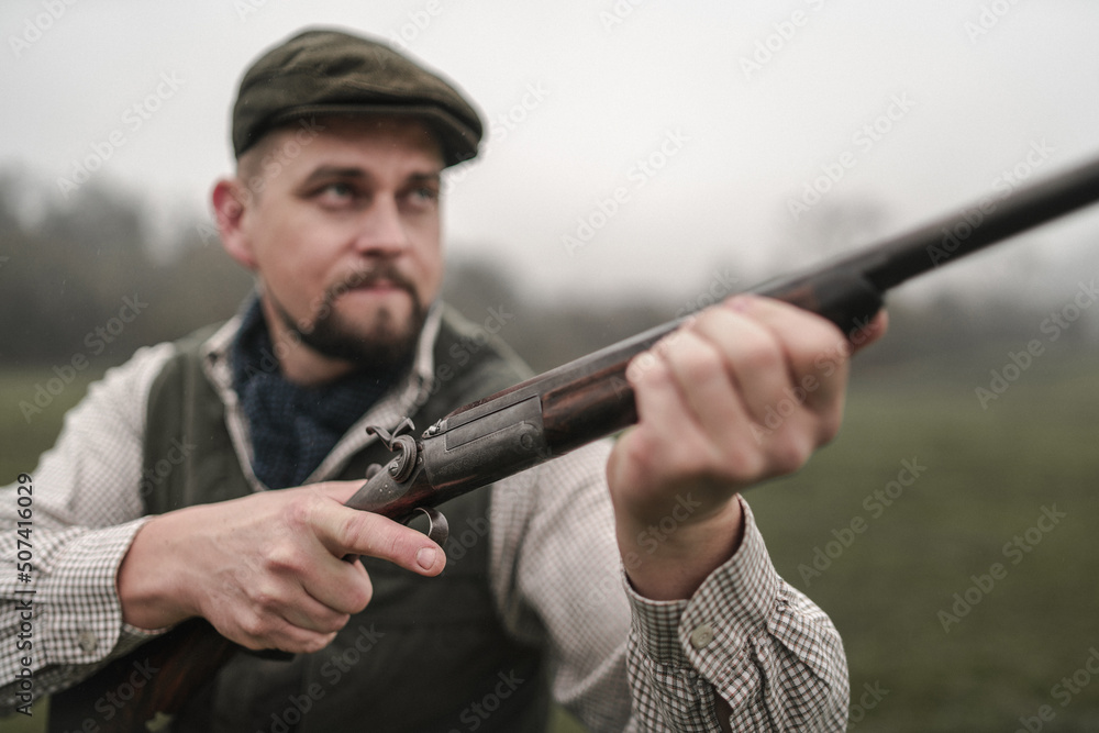 Hunter man in traditional shooting clothes on field aiming with shotgun ...