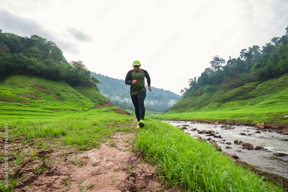 Young Asian men running in nature trails, among forests, valleys and ...