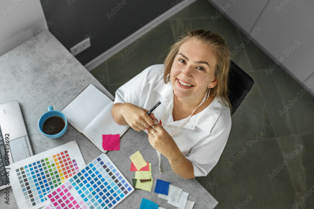 Woman sits at table in modern office next to color palette and fabric ...