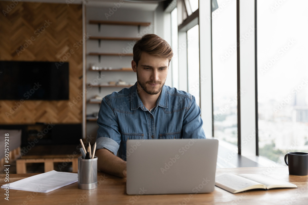 Serious distance employee working from home, using laptop, typing ...
