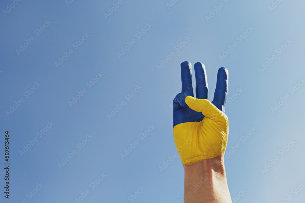Man's hand lit by sunshine painted in colors of Ukrainian national flag ...