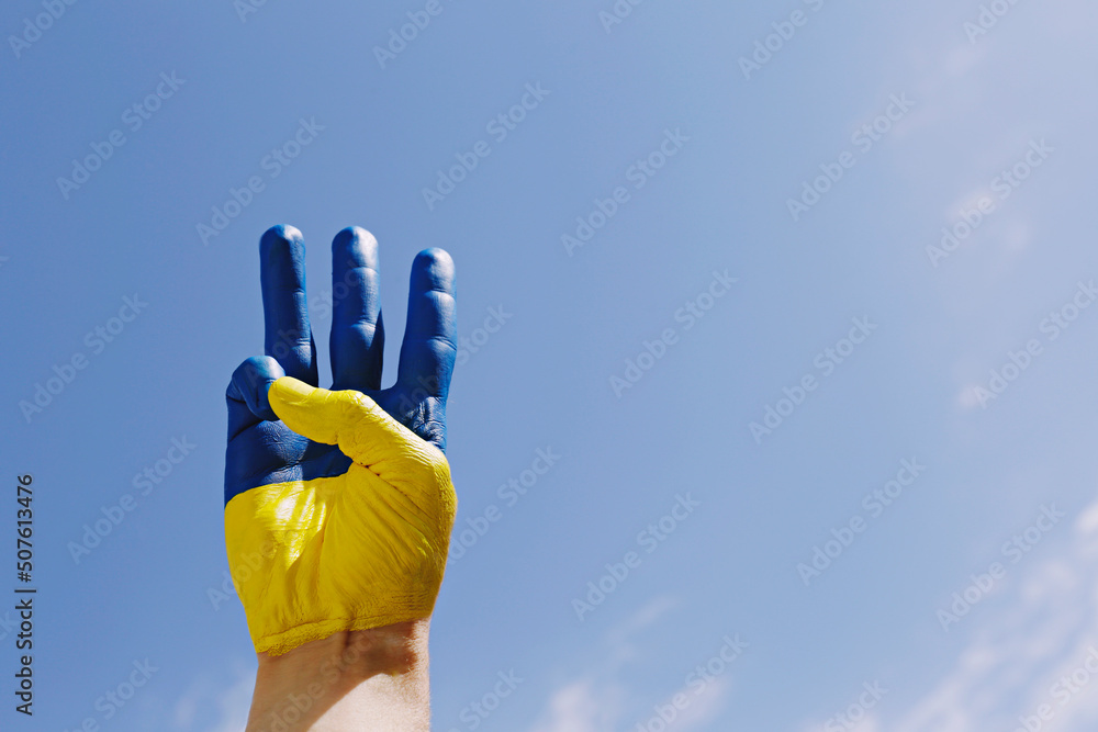 Man's hand lit by sunshine painted in colors of Ukrainian national flag ...