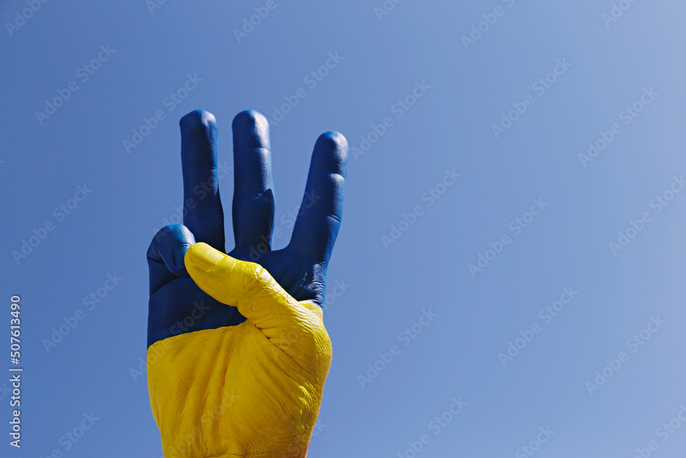 Man's hand lit by sunshine painted in colors of Ukrainian national flag ...