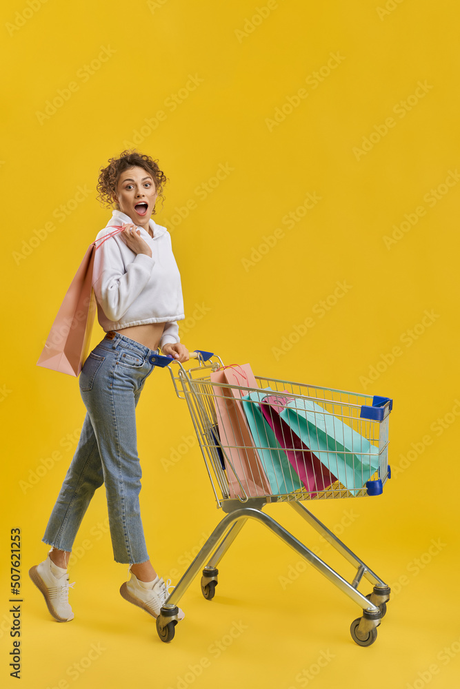 Shocked woman carrying shopping cart, with bright paper bags inside ...