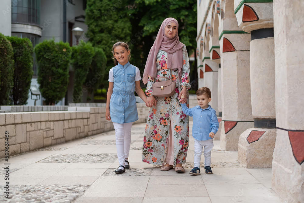 Happy Muslim family mom in hijab walking and holding hands with two ...