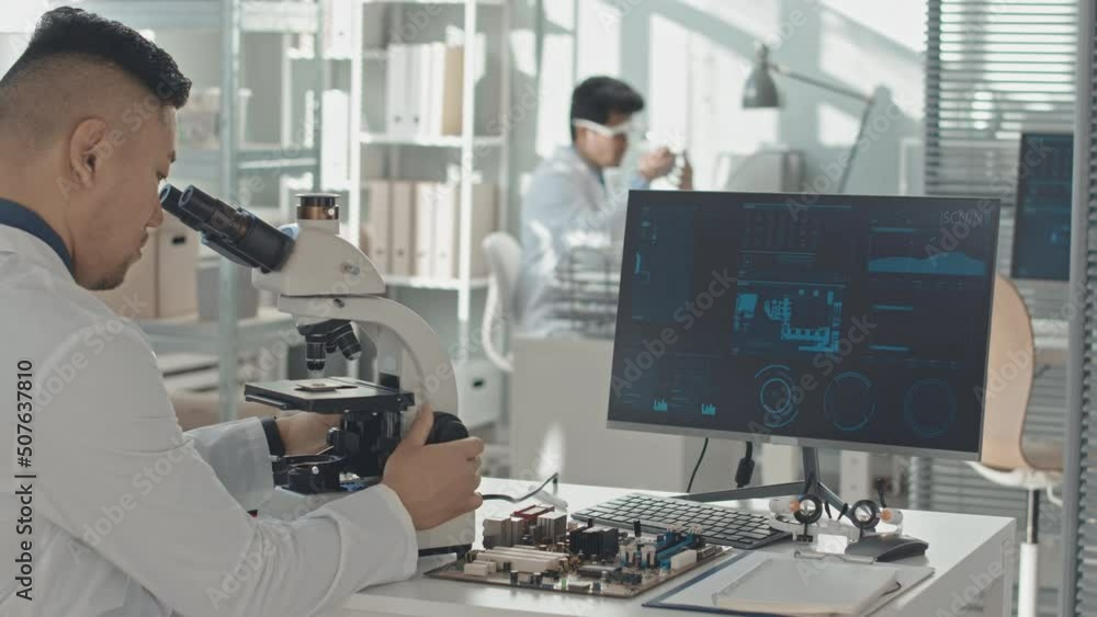 Waist up slowmo of Asian male engineer looking at CPU under microscope ...