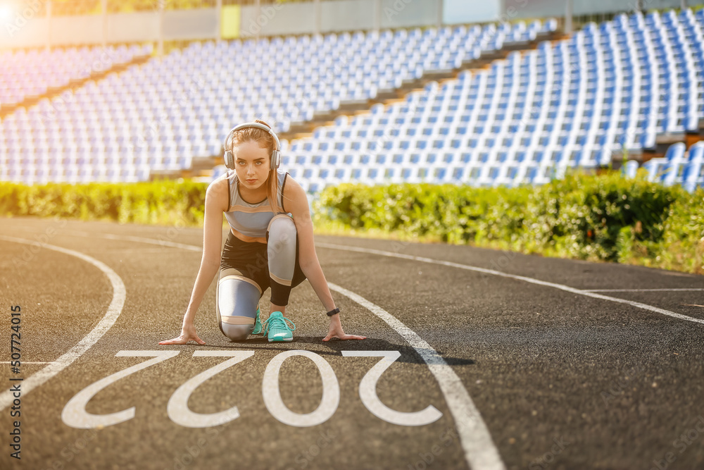 Sporty young woman in crouch start position near figure 2022 on running ...