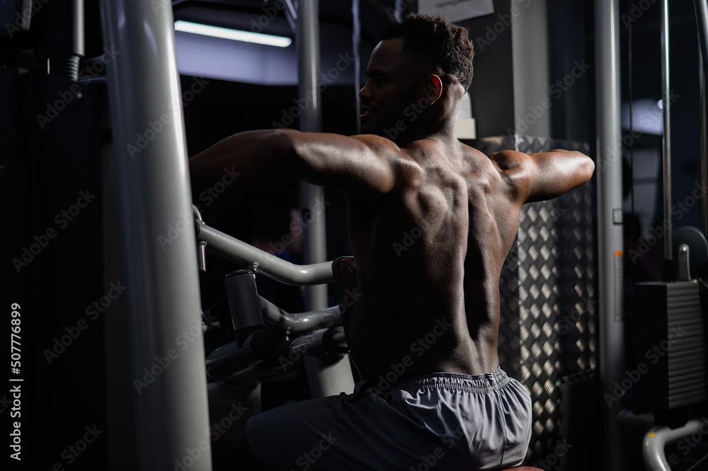 Shirtless african american man doing back exercises on a machine in the ...