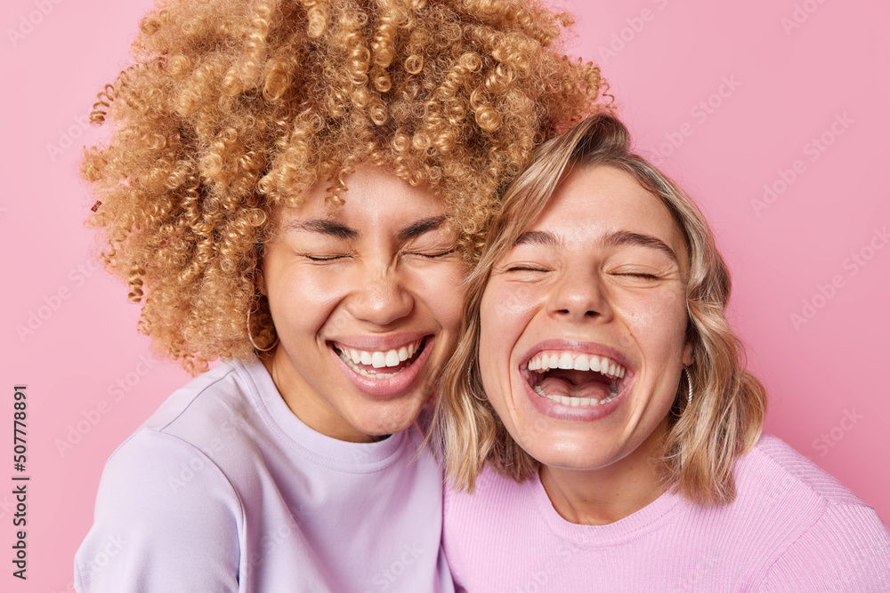 Two overjoyed young women laugh out gladfully keep eyes closed stand ...