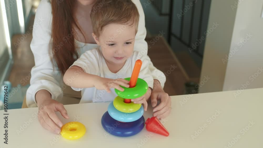 baby collects a toy pyramid. mom plays with son at home happy family ...