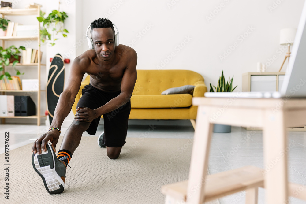 Athletic young adult african man training and stretching while watching ...