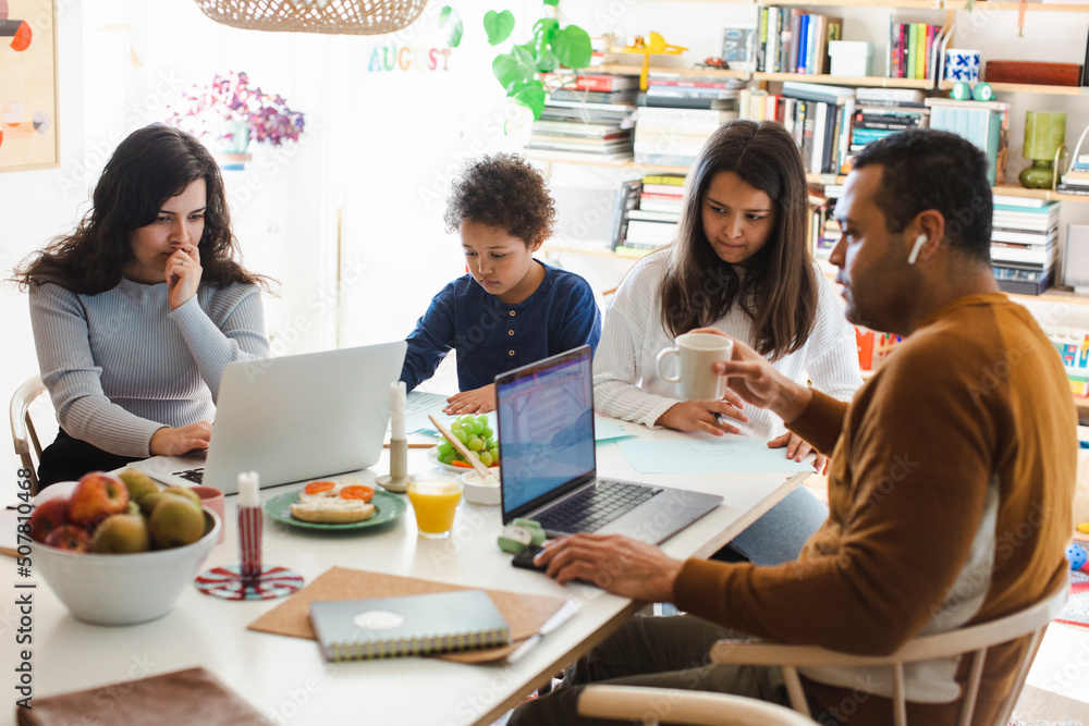 Parents working on laptop while sitting with son and daughter at table ...