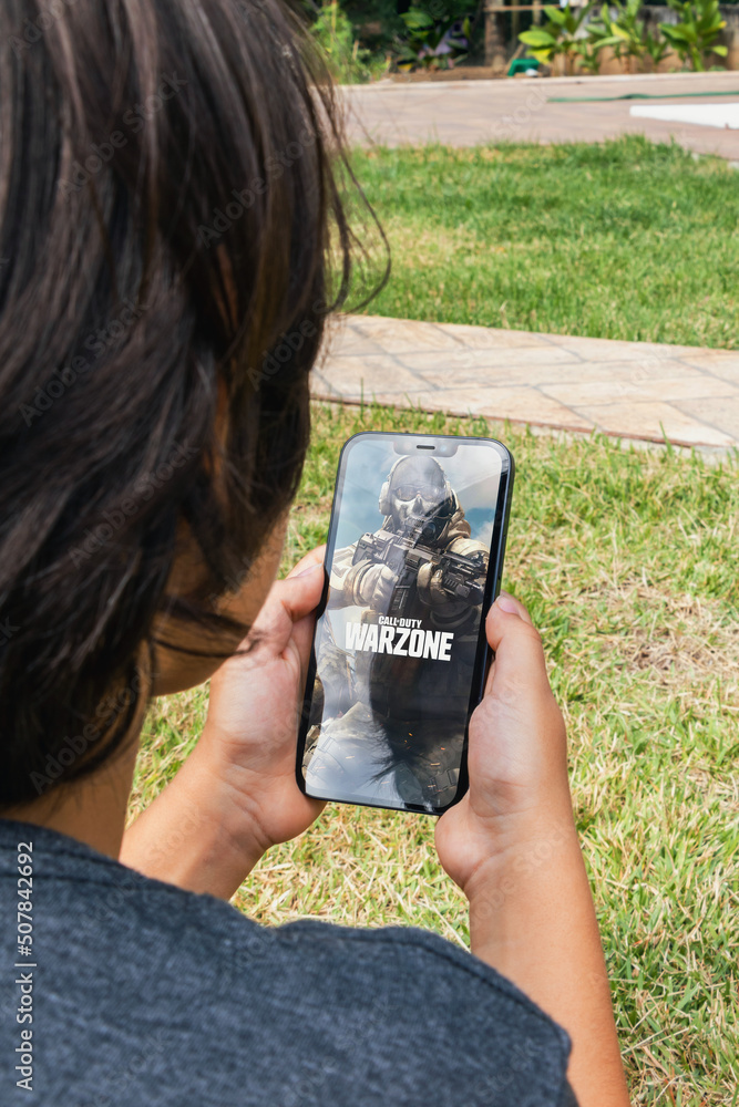 Child sitting on grass with Call of Duty Warzone COD mobile game app on ...