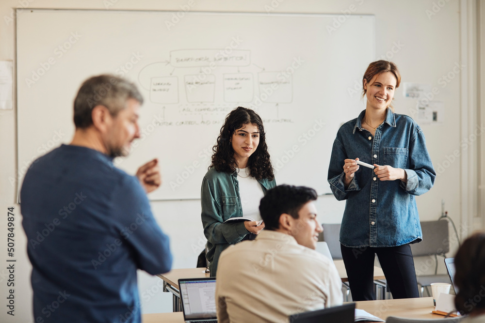 Young female students interacting with friends during lecture in ...