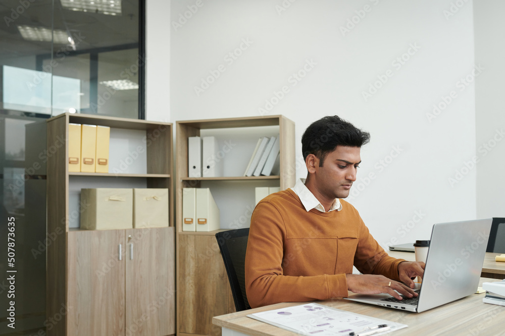Pensive concentrated Indian entrepreneur working on laptop at office ...