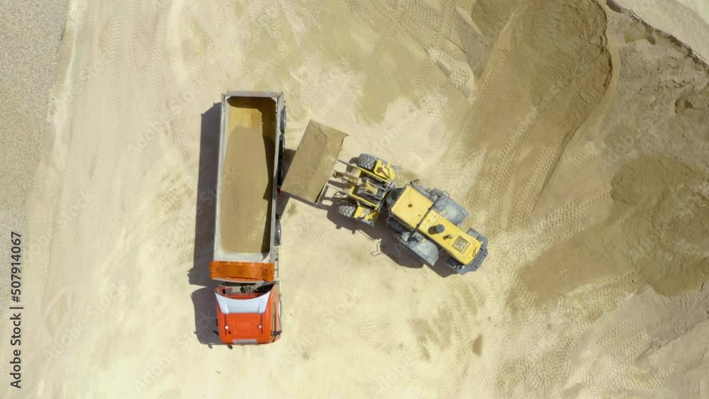 Bulldozer loading a truck with sand at sand extraction area, Aerial top down shot. Aerial top ...
