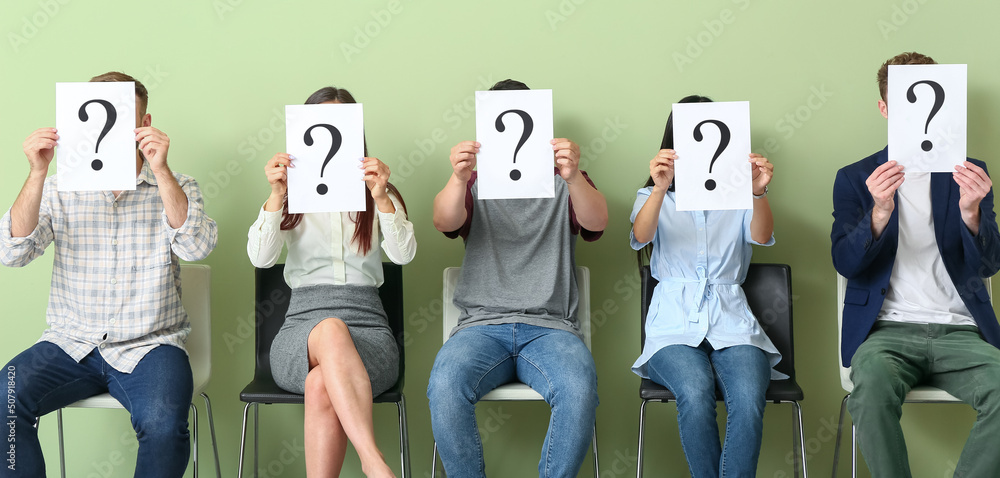 Young people holding paper sheets with question marks while sitting on ...