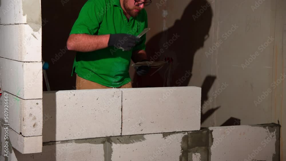 Builder laying a wall of gas blocks with tools and adhesive mortar ...