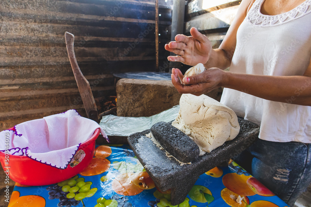 Mujer mexicana torteando maza de maíz en un metate y una estufa de leña ...
