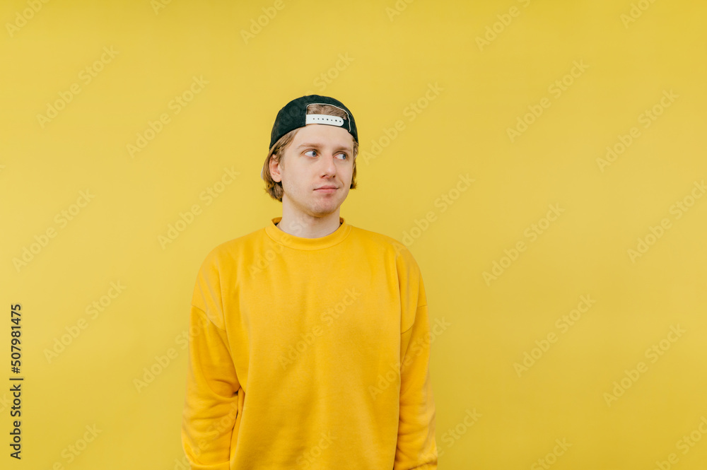 Handsome young man in a cap and yellow sweatshirt stands on a colored ...