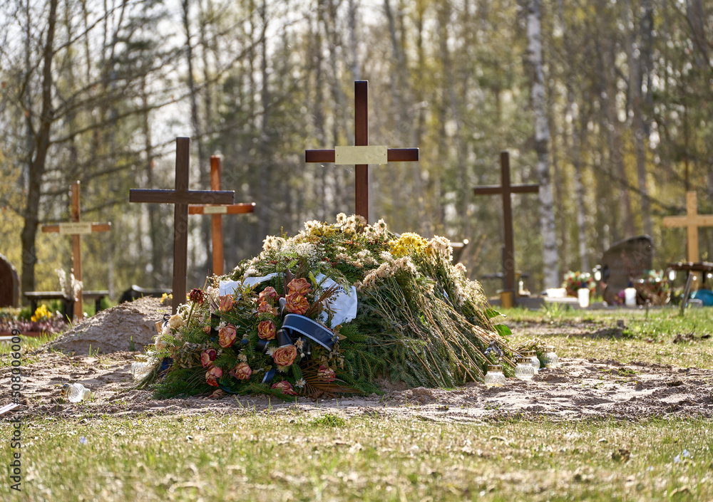 New grave with wooden cross and several funeral wreaths. Another graves ...