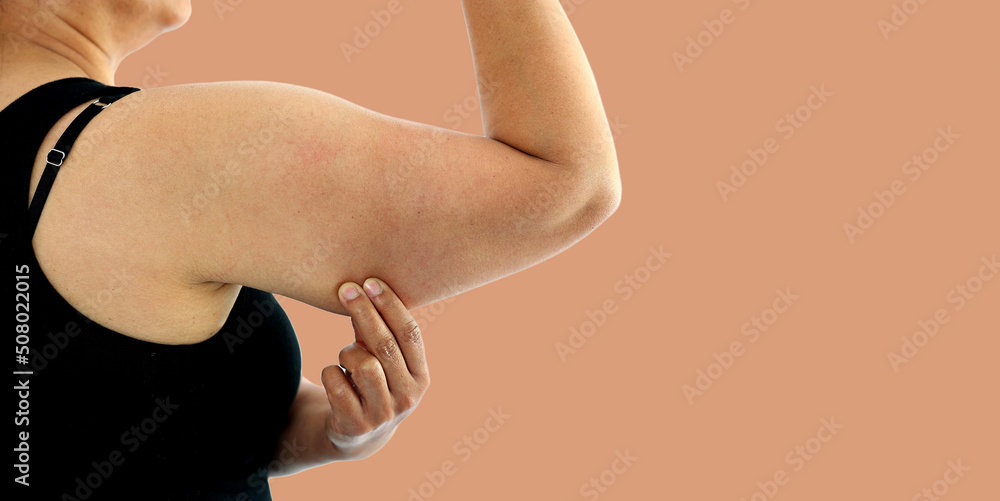A young Asian woman grabbing skin on her upper arm with excess fat ...