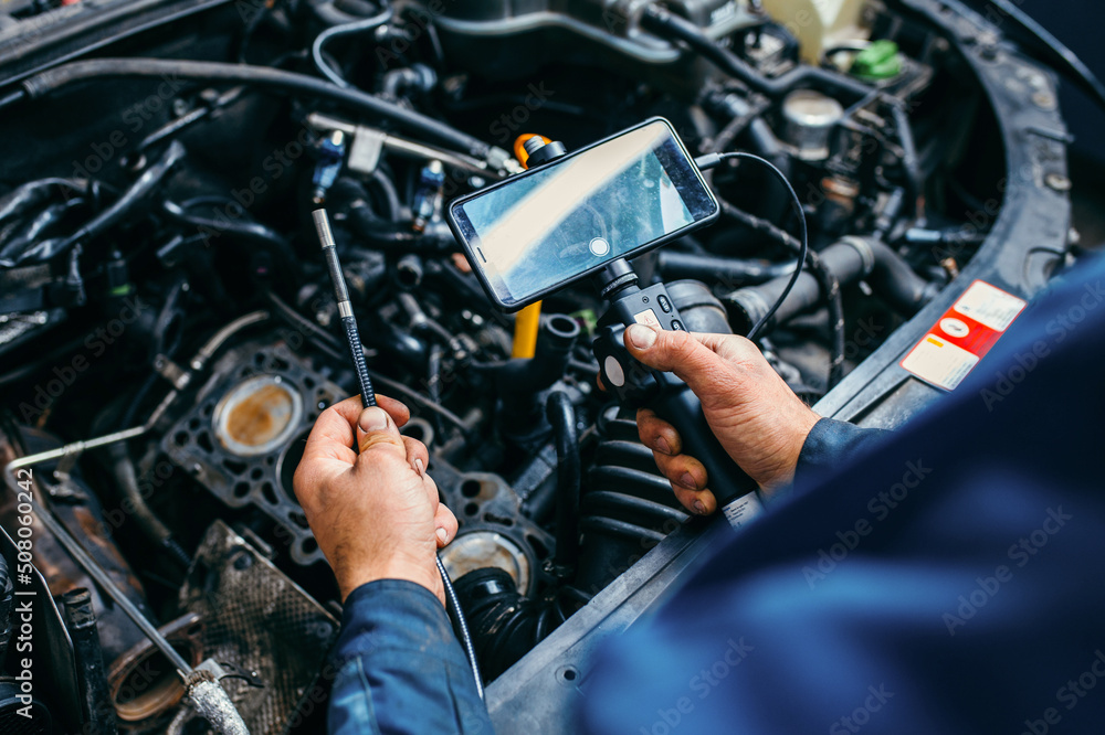 Hands of car mechanic check the vehicle engine with technical endoscope ...