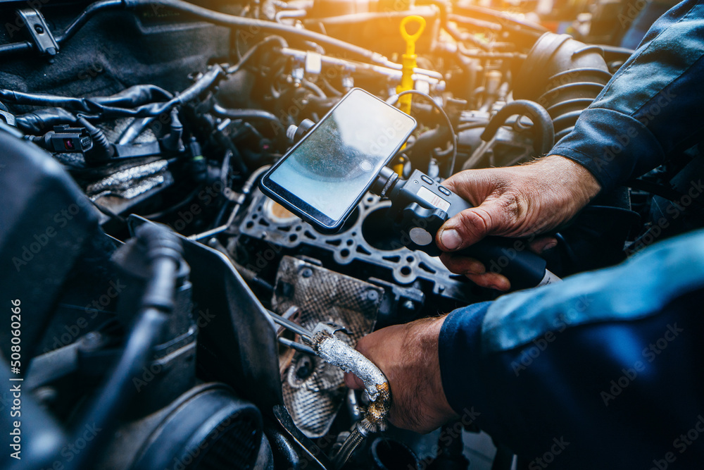 Hands of car mechanic check the vehicle engine with technical endoscope ...