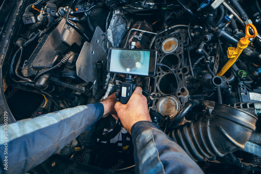 Hands of car mechanic check the vehicle engine with technical endoscope ...