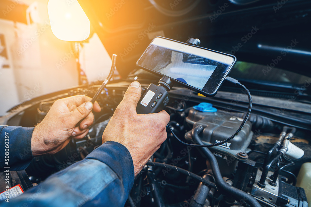 Hands of car mechanic check the vehicle engine with technical endoscope ...