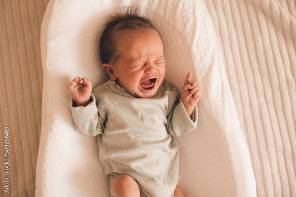 Unhappy sad baby lying in bed crib wake up and crying at home in room ...