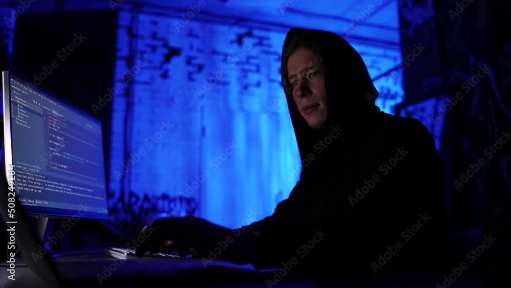 Low-angle side view of dangerous hacker man in sweatshirt typing code ...