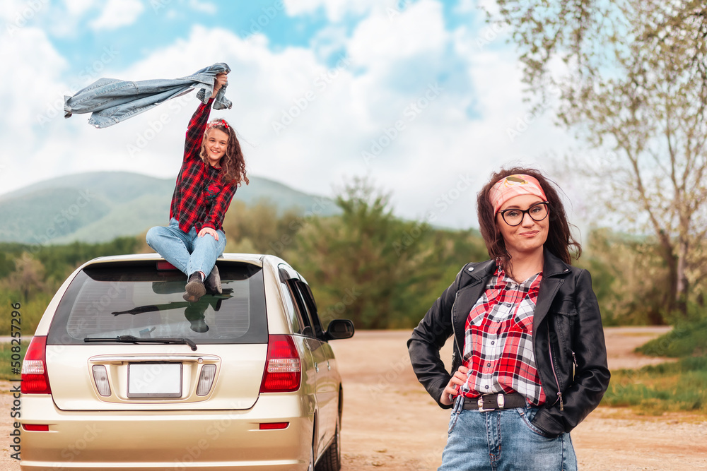 Happy teen girl is sitting on the roof of a car, joyfully raising her ...