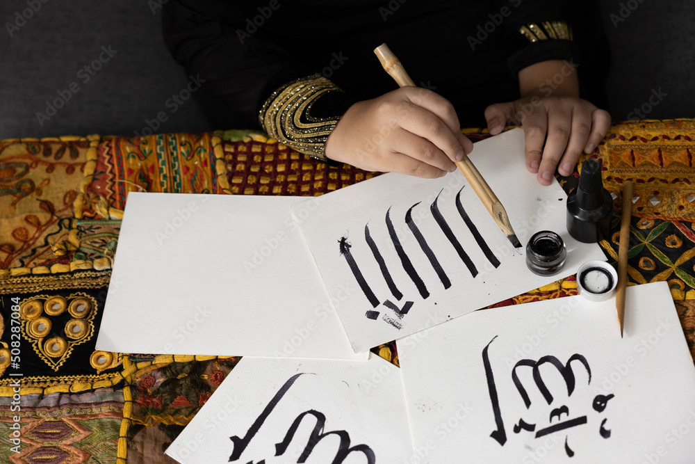 close up muslim girl hands writing Arabic text with bamboo pens and ...