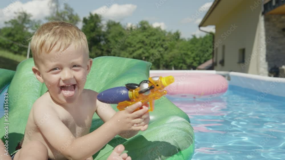CLOSE UP: Little boy enjoying at water fight game while floating in ...