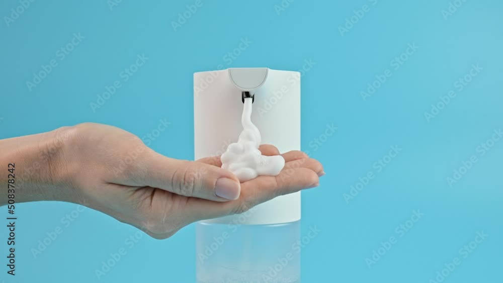 Using an automatic soap dispenser. Young girl woman brings her hands to ...
