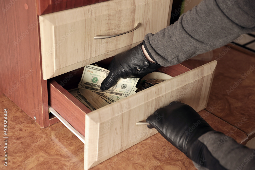 Robber in black outfit and gloves see in opened shelf in kitchen. The ...