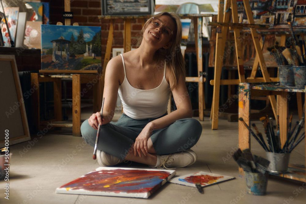 Horizontal image of a pretty female artist sitting on the floor in the ...