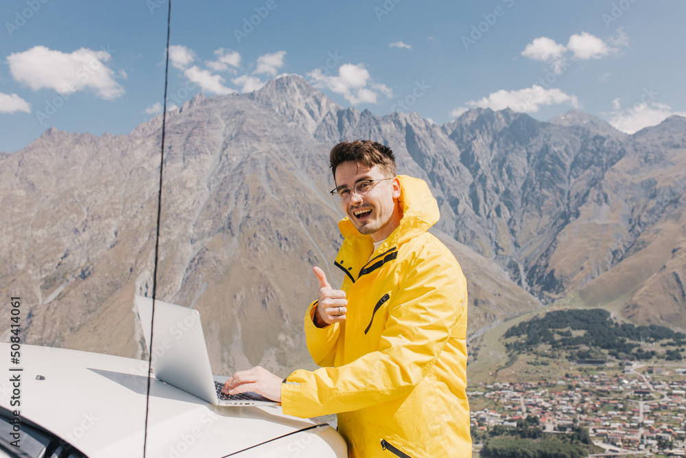 Backpacker working remotely on the hood of his SUV while in the ...