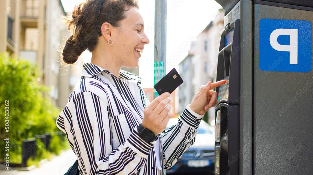 Happy elegant young woman pay for ticket in parking meter, holding ...