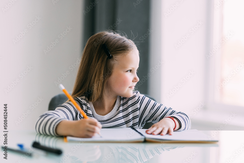 Cute little girl doing homework, reading a book, coloring pages ...