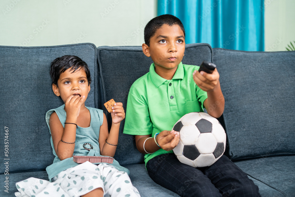 sibling kids busy watching television or tv by sharing biscuits at home ...