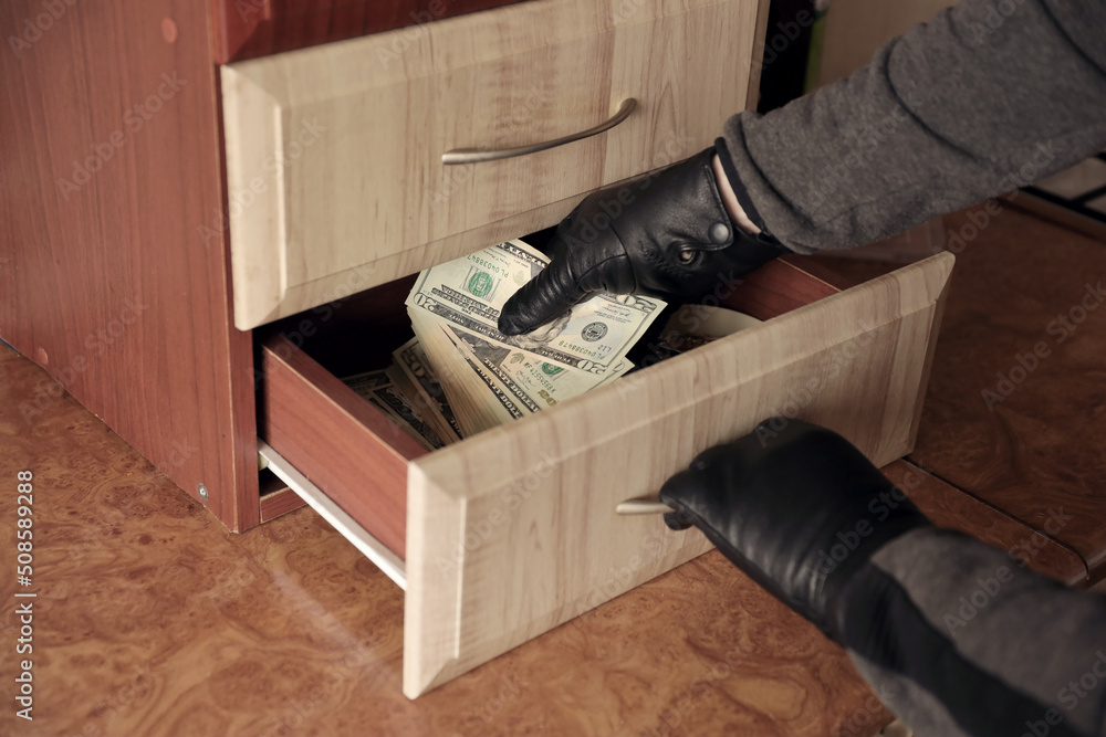 Robber in black outfit and gloves see in opened shelf in kitchen. The ...