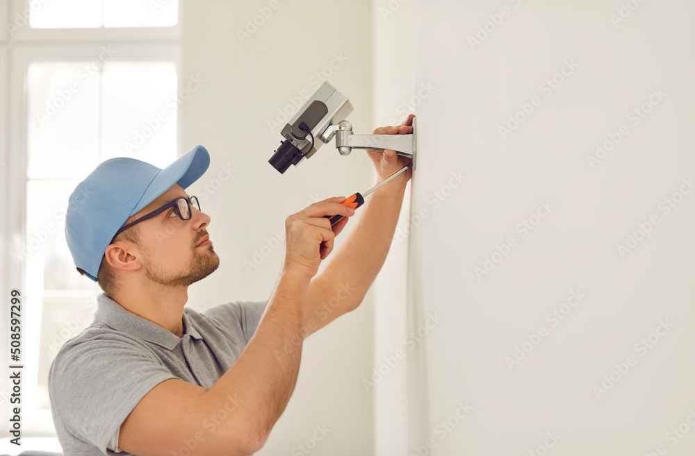 Professional male surveillance camera installer mounts it on wall ...