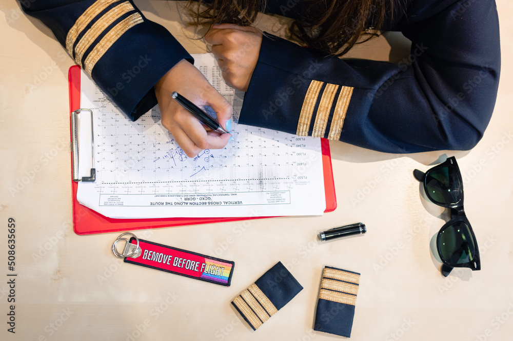Unrecognizable female pilot preparing flight documentation with a Remove Before Flight keychain ...