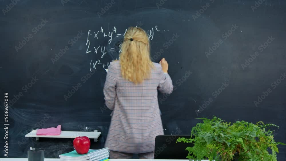 Math teacher writes examples for school children on blackboard. Student ...