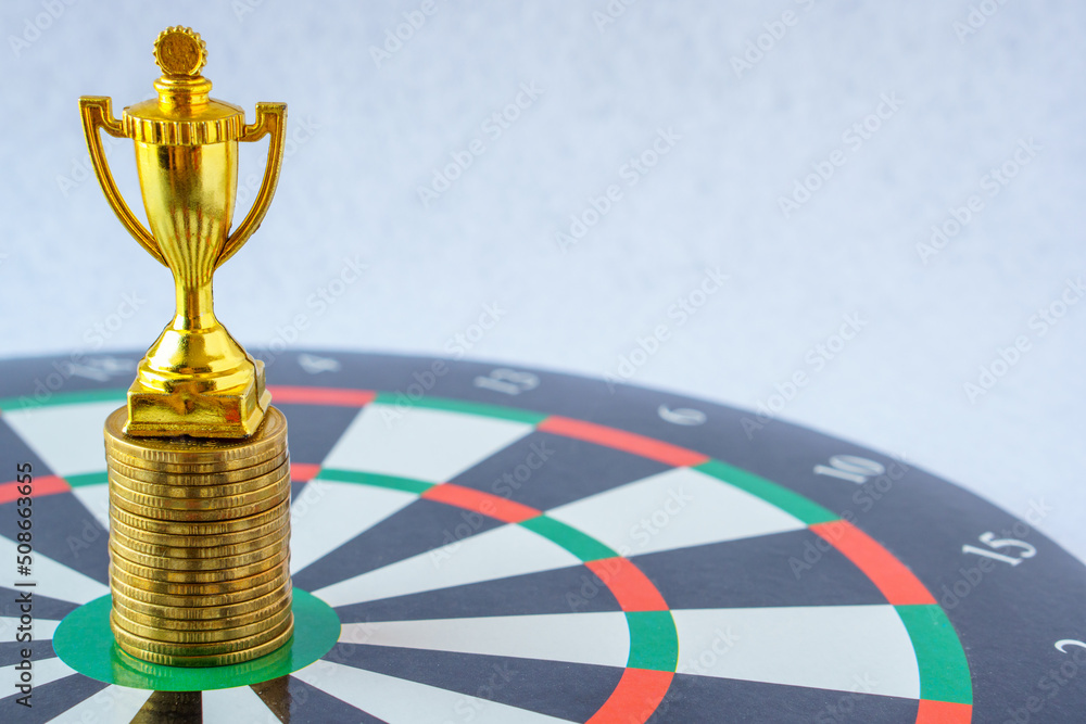 gold trophy and stack of gold coin on dartboard hitting in the target ...