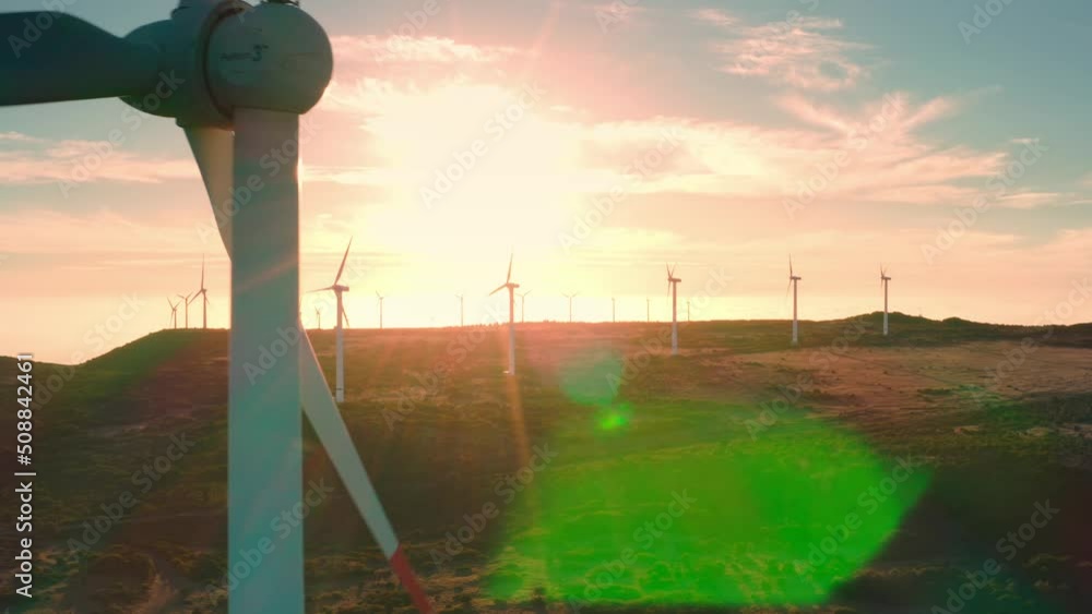 close up moving wind turbine at the sunset and many windmills at the ...